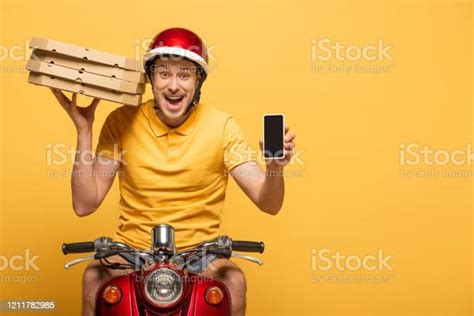 피자 상자와 노란색 유니폼 승마 스쿠터에 흥분 배달 남자와 노란색에 고립 된 빈 화면스마트 폰을 보여주는 배달에 대한 스톡 사진