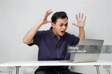 Angry Mad Asian Man In Workplace While Sitting In Front Of Laptop