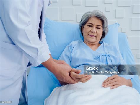 행복한 아시아 노인 환자 여성이 침대에서 웃고있는 동안 흰색 실험실 코트를 입은 의사가 병원 회복실에서 심장 박동 맥박을 검사하기 위해 손을 잡고 있습니다 의료 건강 관리