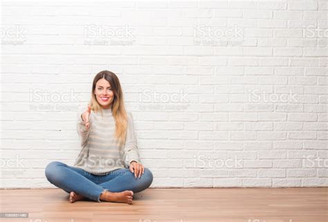 젊은 성인 여자 집에서 흰색 벽돌 벽을 통해 바닥에 앉아 미소 인사와 환영으로 제공 하는 친절 한 악수 성공적인 사업입니다