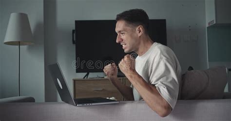 Seated On Couch Man Works On Laptop Face Lighting Up With Sense Of