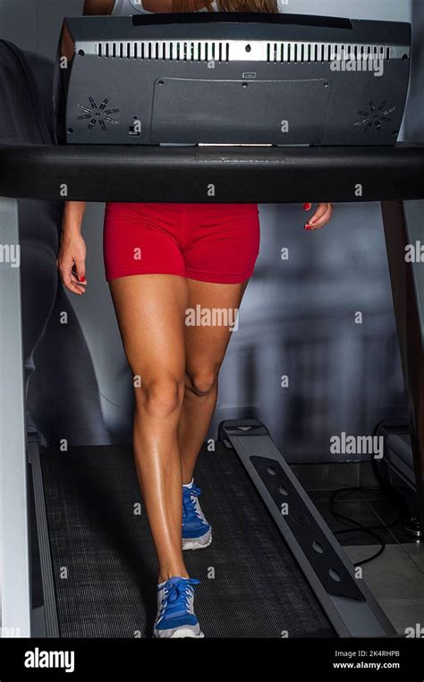 Legs Of Woman In Red Shorts And Blue Sneakers Walking On A Treadmill At