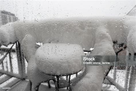 흐린 날에는 창문 유리에 얼음이 떨어지며 선택적 초점 겨울에는 창문을 통해 눈 덮인 테이블과 의자가 있는 테라스의 전망을 감상하실 수 있습니다 자연 재해 얼어붙은 비 서리