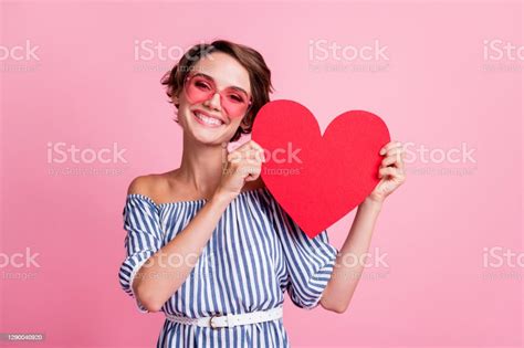 파스텔 핑크 컬러 배경에 고립 된 장미 색 안경을 착용 하는 두 손으로 큰 빨간 하트 카드를 들고 귀여운 여자의 사진 초상화