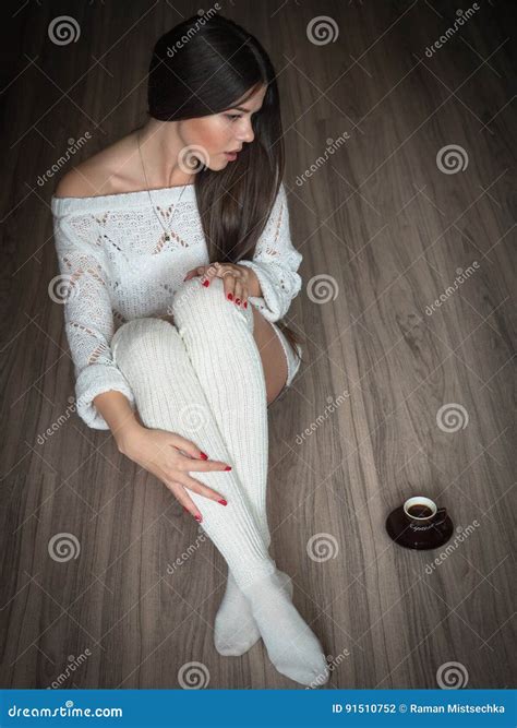 Girl With White Sweater And Socks Is Sitting On A Hardwood Floor With