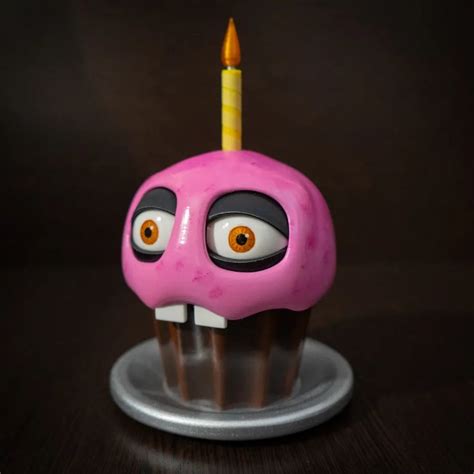 A Pink Cupcake With A Candle Sticking Out Of Its Mouth On A Plate