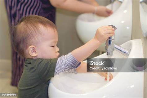 귀여운 작은 아시아 18 개월 1 년 오래 된 유아 아기 소년 아동 세척 청소 공공 화장실에 수도 꼭지에서 흰색 싱크대와 물 하락에 혼자서 손 화장실 건축물에 대한 스톡