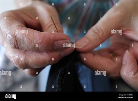 The Hands Of A Senior Woman Who Uses Needle And Thread To Repair A