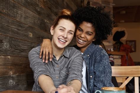 Duas Lésbicas Alegres Rindo E Se Abraçando Enquanto Tomam Café