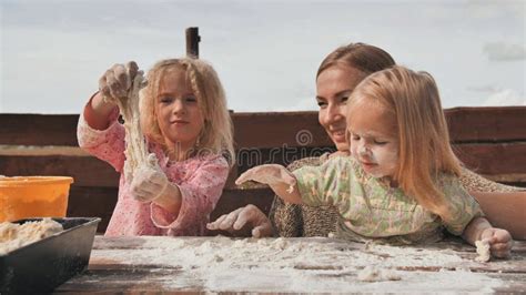 Two Daughters Knead The Dough With Their Hands Next To Their Mother
