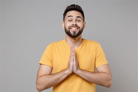 젊은 백인 수염 행복한 매력적인 남자 20 대 캐주얼 노란색 기본 티셔츠 손을 입고 기도 제스처에 접혀 회색 색상 배경 스튜디오 초상화에 고립 된 무언가에 대해 구걸 T