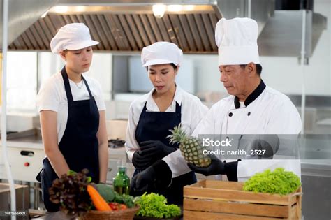 팀 셰프가 주방에서 함께 음식을 위해 신선한 야채를 요리하고 준비하는 방법에 대해 설명하고 견습생을 설명하고 남자는 레시피 식사 준비에 대해 조수 여성을 훈련하고 토론합니다