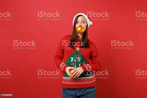 스웨터 크리스마스 모자 들고 노란색 나무 장난감 붉은 배경에 고립 된 손과 입에 매력적인 젊은 산타 소녀 행복 한 새 해 2019 축 하 휴일 파티 개념입니다 복사 공간을
