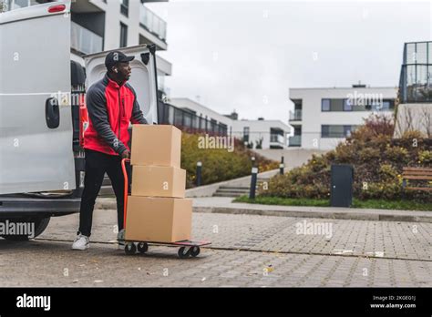 Black Young Adult Delivery Guy In Work Uniform Unloading Cardboard Box
