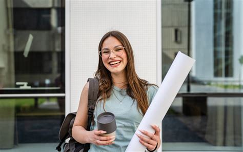 한 여성 젊은 성인 백인 여학생이 종이와 커피 한 잔을 들고 대학 앞에 서서 밝은 날 행복한 미소를 지으며 카메라를 바라 보는 실제 사람들이 공간을 복사합니다 학생에 대한