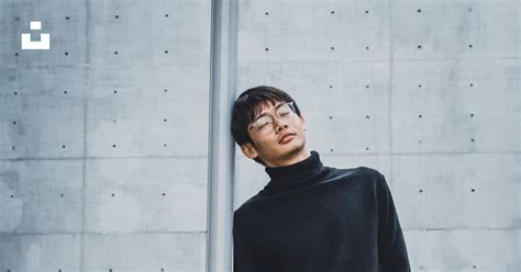 검은 스웨터와 파란색과 흰색 격자 무늬 바지를 입은 남자가 흰색 콘크리트 벽 옆에 서 있습니다 사진 Unsplash의 무료