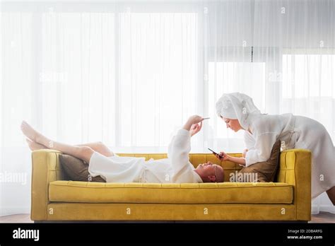 Couple In Bathrobes Is Relaxing On The Yellow Sofa With Mobile Phone