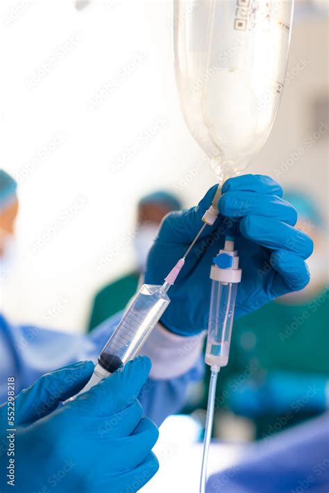 Vertical Of Gloved Hand Of Surgical Tech Preparing Iv Bag In Operating