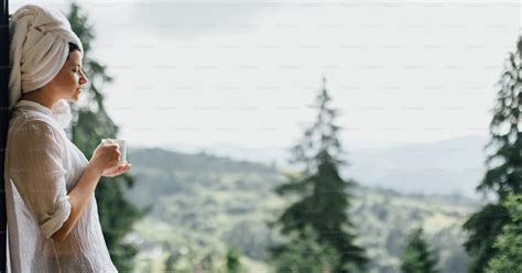 산 언덕을 배경으로 화창한 아침에 뜨거운 커피를 즐기는 아름다운 관능적인 여자 차분한 순간 복사 공간 샤워 후 흰 셔츠와 수건을 입은 젊은 여성이 커피 한 잔과 함께