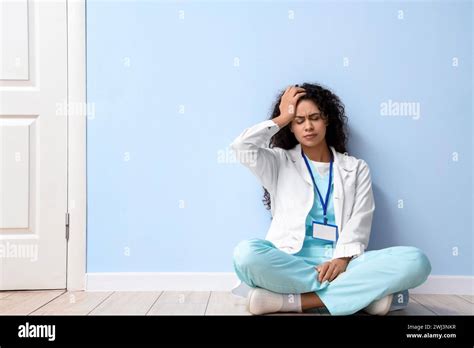 Stressed Female African American Medical Intern Sitting Near Blue Wall