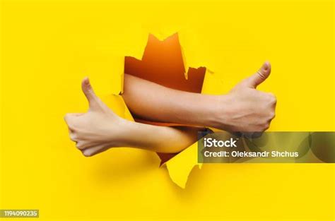좋아요 남자와 여자의 손의 사인을 엄지 손가락 손목은 노란 종이에 찢어진 구멍을 통해 나왔고 손가락을 위아래로 보여줍니다 좋은