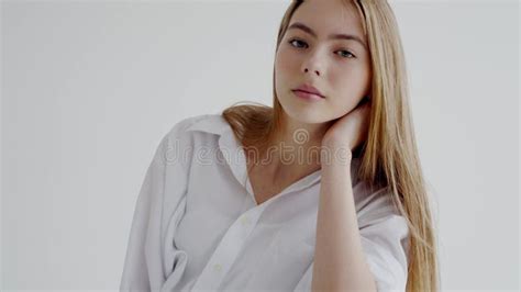 Young Woman In White Shirt Posing Elegantly Against Plain Background