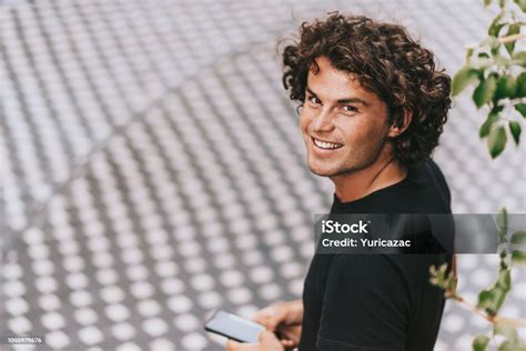 검은 티셔츠에 밝은 사람의 후면 보기 이미지는 거리에 그의 휴대 전화에 문자 메시지를 읽고 젊은 백인 남자 곱슬 머리 텍스트 복사 공간을 가진 카메라를 찾고 모던 양식에