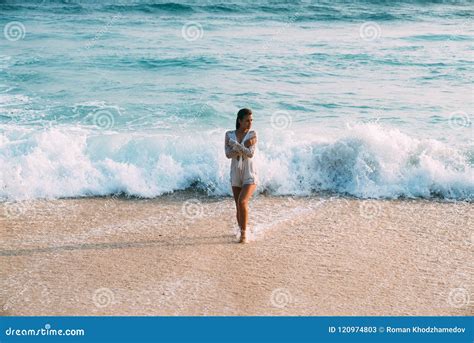 Una Bella Ragazza Esile E Suntanned Sexy In Un Vestito Bianco Dalla Spiaggia Sta Stando Bagnata