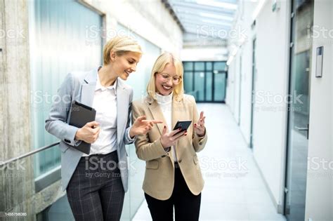 복도에 서서 스마트폰을 보고 있는 두 명의 쾌활한 사업가 동료의 초상화 25 29세에 대한 스톡 사진 및 기타 이미지 25