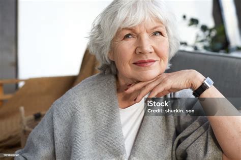 우아함 나이 아름다움과 사람들의 개념입니다 집에서 자유 시간을 즐기고 매력적인 우아한 수석 성숙한 여자의 실내 이미지 세련 된 거실 인테리어에 소파에 앉아 행복 하 게 웃