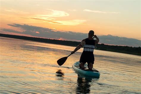 A Man In Shorts With His Back To The Camera On His Knees On A Sup Board