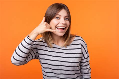 전화하세요 긴 소매 줄무늬 셔츠에 갈색 머리와 명랑 아름다운 여자의 초상화 오렌지 배경에 고립 된 실내 스튜디오 샷 20 29