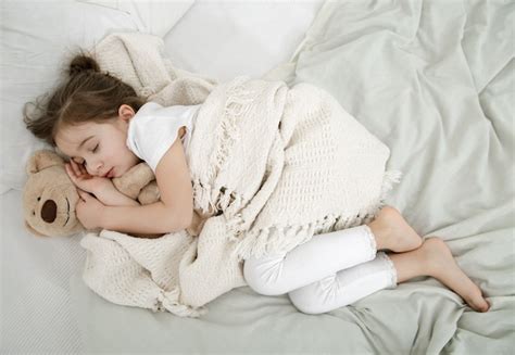 Uma Linda Menina Está Dormindo Em Uma Cama Com Um Ursinho De Pelúcia
