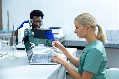Female Chemist In Lab Discussing With Multiethnic Colleagues Using