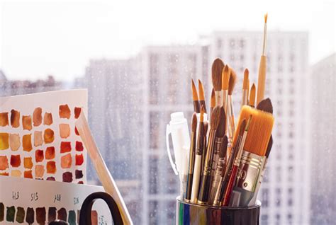 봄철 햇볕이 잘 드는 도시를 배경으로 더러운 창문에 다양한 브러시가 서 있습니다 근처에는 손으로 그린 수채화 팔레트가있는 종이 한 장이 있습니다 창의적인 개념 0명에 대한