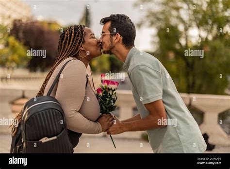 Young Couple Kissing Each Other With Bouquet Of Flowers At Footpath