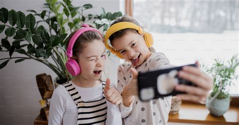 집에서 실내에서 헤드폰을 끼고 셀카를 찍을 때 얼굴을 찡그린 두 명의 쾌활한 작은 소녀 자매 사진 Unsplash의 헤드폰 이미지