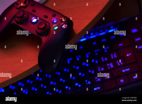 Modern Gamepad Lies With Pc Keyboard On Table In Dark Playroom Scene Close Up Video Game