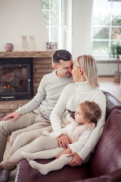 The Family Sits On The Couch Near The Fireplace Mom Dad Babe And Cat In The Home Interior
