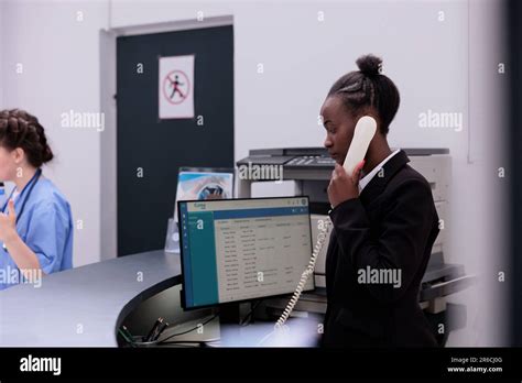 Receptionist Talking At Landline Phone With Remote Patient Discussing