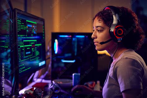 Female Teenage Hacker Sitting In Front Of Computer Screens Bypassing Cyber Security Stock Photo