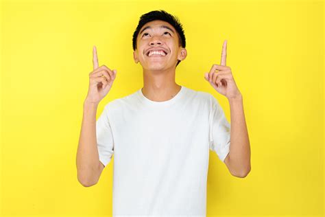 친근한 모습의 활기찬 활기찬 아시아 남성 흰색 티셔츠 미소 는 카피 공간 즐거운 모습 자기 확신 포인팅 T 셔츠에 대한 스톡