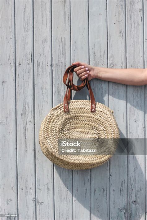 젊은 백인 여성의 클로즈업 은 가죽 스트랩라운드 밀짚 가방을 들고 손 창백한 늙은 초라한 페인트 나무 질감문 배경 여름 방학