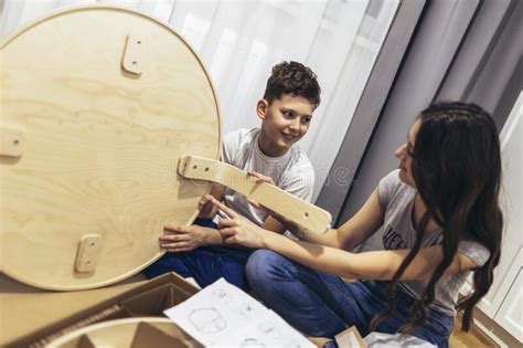 Brother And Sister In Casual Clothing Assembling Furniture In Apartment