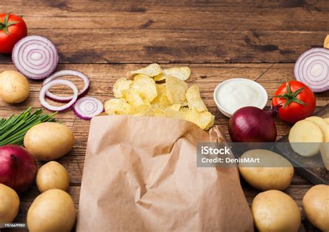 신선한 유기농 홈메이드 감자 감자칩 칩과 사 워 크림과 빨간 양파 그리고 나무 배경에 종이 봉지에 향신료가 있습니다 신선한 노란