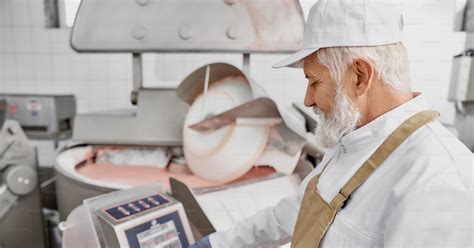 흰색 유니폼 흰색 모자 갈색 앞치마 고무 장갑을 끼고 육류 생산 라인에서 일하는 노인 노동자 고기를 갈기 위해 장비 근처에 서 있는 작업자 사진 Unsplash