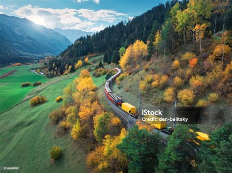 스위스 알프스 계곡의 노란색 화물 마차가 있는 현대적인 빨간색 기차의 공중 전망 베르니나 익스프레스 열차 산 푸른 초원 가을에 노란 나무의 평면도 철도 여행 기차에 대한