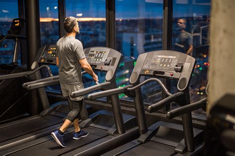 헬스 클럽에 디딜 방 아에 걷는 수석 남자의 전체 길이입니다 밤 하루 시간대에 대한 스톡 사진 및 기타 이미지 밤 하루