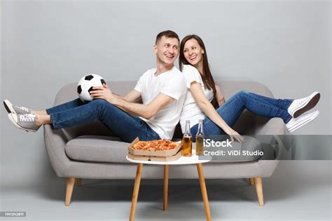 즐거운 커플 여자 남자 축구 팬 응원 축구 공 회색 벽 배경에 고립 된 뒤에 다시 앉아 좋아하는 팀 지원 사람들의 감정 스포츠 가족 레저 라이프 스타일 개념입니다