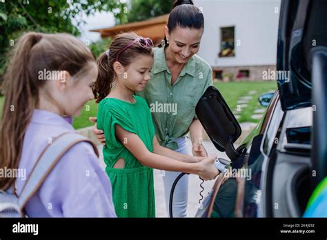 Happy Mother Showing Her Little Daughters How To Charge Their Electric